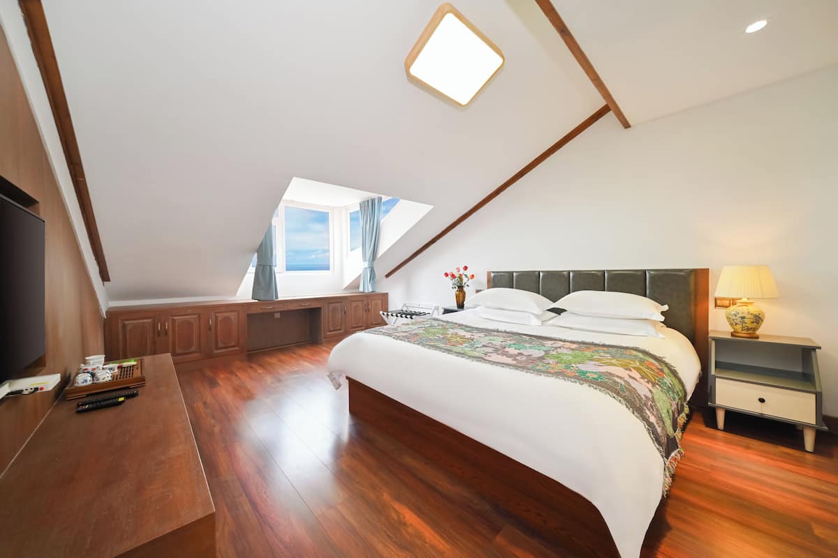 Quarto com cama grande, escrivaninha, televisão e janela com vista.