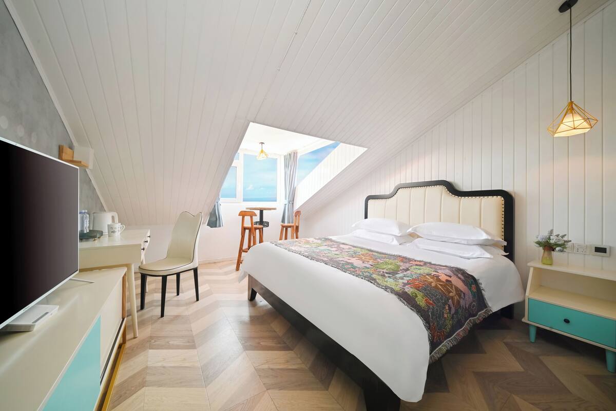 Quarto com cama, escrivaninha, cadeira e televisão.