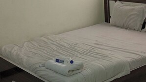 Quarto com cama, ar condicionado, janela com cortinas e mesa de cabeceira com uma garrafa.
