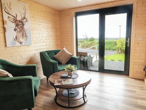 Um interior em madeira com um sofá verde, uma mesa com revistas e um quadro de um veado.