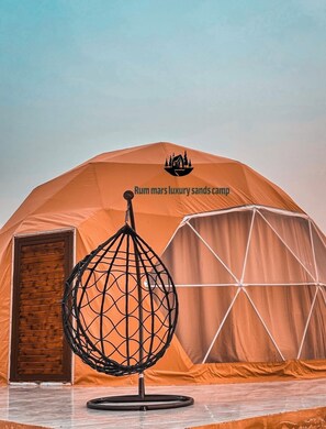 Uma tenda com um logotipo e o texto 'Rum mars luxury sands camp' e uma cadeira suspensa na frente.