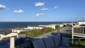 Vista para o mar com uma fileira de casas móveis brancas, um carro estacionado e um carro azul em primeiro plano.