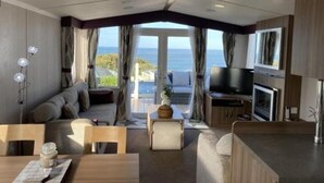 Interior moderno de um veículo recreativo, com sofá, mesa de jantar, televisão e vista para o oceano.