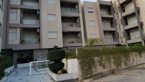 Um edifício residencial com vários andares, varandas, portão fechado e entrada pavimentada.