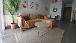 Uma sala de estar com sofá, mesa de centro redonda, planta em vaso e obras de arte na parede.