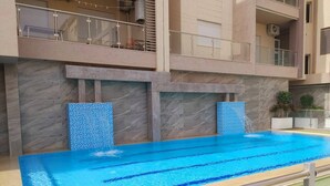 Piscina com deck revestido em azulejo, parede de mármore e varanda com corrimão.