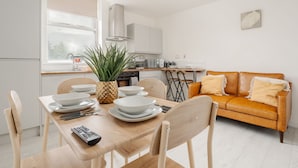 Uma cozinha moderna com armários brancos, uma mesa de jantar posta com pratos e tigelas, um sofá e um vaso de planta.