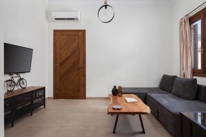 Uma sala de estar moderna com porta de madeira, TV sobre suporte, sofá, mesa com um vaso e luminária pendente.