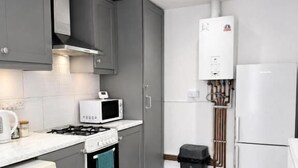Uma cozinha moderna com armários cinza, uma geladeira branca, micro-ondas, fogão e aquecedor de água.