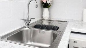 Uma cozinha com uma pia de aço inoxidável, um escorredor de louça e um vaso branco com flores.
