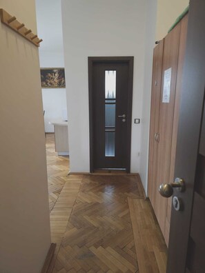 Um corredor com piso de madeira, porta escura e um guarda-roupa de madeira com fechadura.