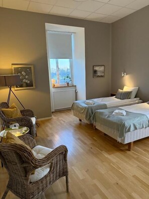 Quarto com duas camas, uma cadeira, uma mesinha, uma janela e um radiador.