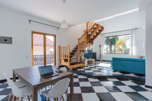 Um interior moderno com escada de madeira, área de refeições com um laptop e um sofá azul.