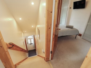Escada que leva a um quarto com cama, televisão e porta de madeira.