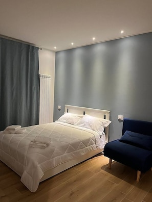 Quarto com cama, cadeira, radiador e cortina.