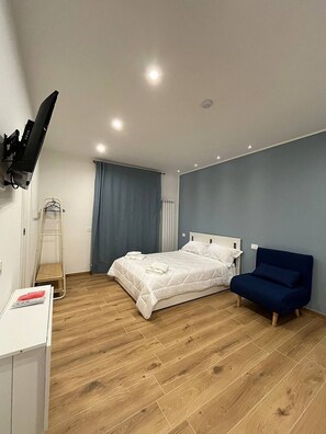 Um quarto com uma cama, uma cadeira azul, uma televisão na parede e um radiador.
