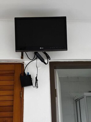Uma TV de tela plana fixada na parede, conectada a uma régua de tomadas por cabos.