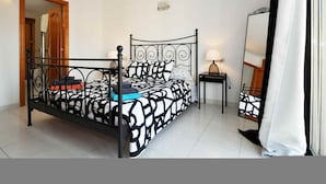 Quarto com cama de dossel, mesa de cabeceira com abajur, espelho e porta que dá para outro cômodo.