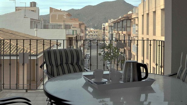 Uma varanda com mesa, cadeiras e vista para a rua e montanhas.