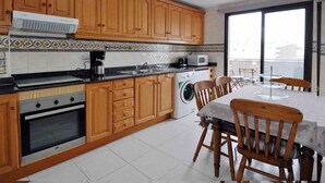 Uma cozinha com armários de madeira, máquina de lavar, micro-ondas e um espaço de jantar com mesa e cadeiras.