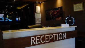 Balcão de recepção com a placa 'RECEPTION', um certificado emoldurado, um relógio e um quadro na parede.