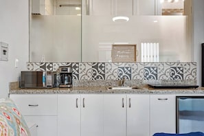 Uma cozinha moderna com micro-ondas, cafeteira e torradeira na bancada, uma pia e um letreiro com a mensagem 'Welcome + HOME' acima do espelho.