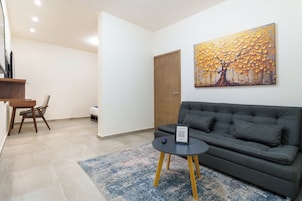 Uma sala de estar moderna com um sofá cinzento, uma pequena mesa redonda com um código QR, uma pintura de uma árvore e uma porta de madeira.