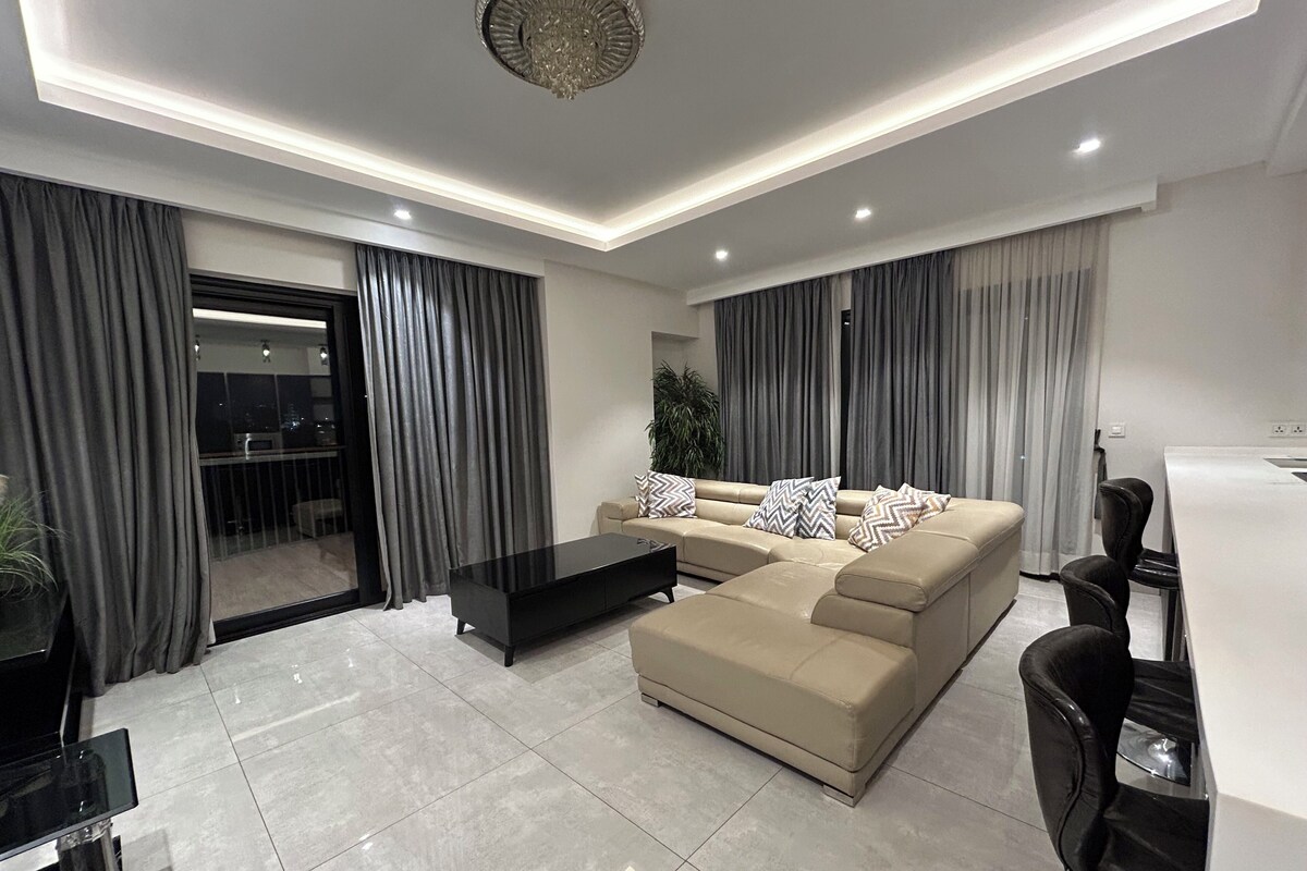 Uma sala de estar moderna com um sofá seccional, uma mesa de centro preta e um espaço de jantar com mesa branca e cadeiras pretas.