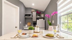 Cozinha moderna com bancada de mármore, geladeira, micro-ondas e janela com vista para o verde.