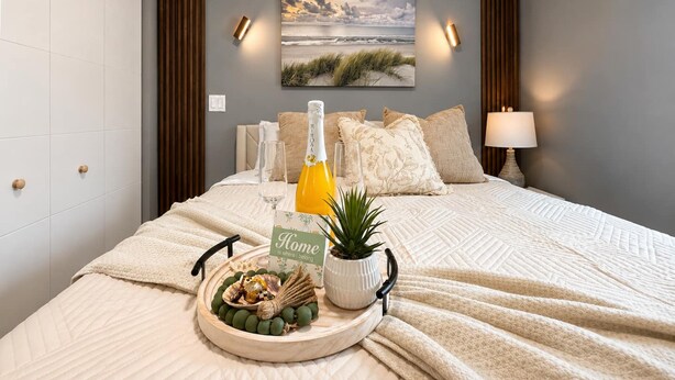 Cama bem arrumada com uma bandeja de itens de café da manhã, um quadro na parede e um abajur.