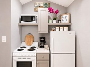 Uma cozinha compacta com micro-ondas, fogão, geladeira e cafeteira.