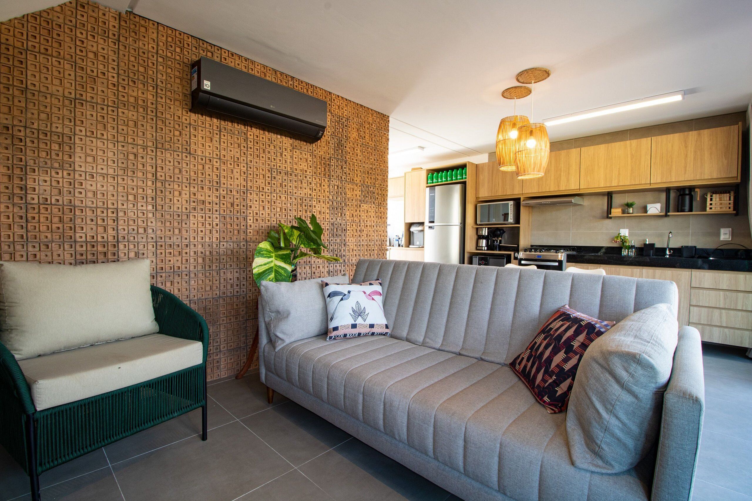 Uma sala de estar moderna com sofá, uma poltrona, parede estampada e cozinha ao fundo.
