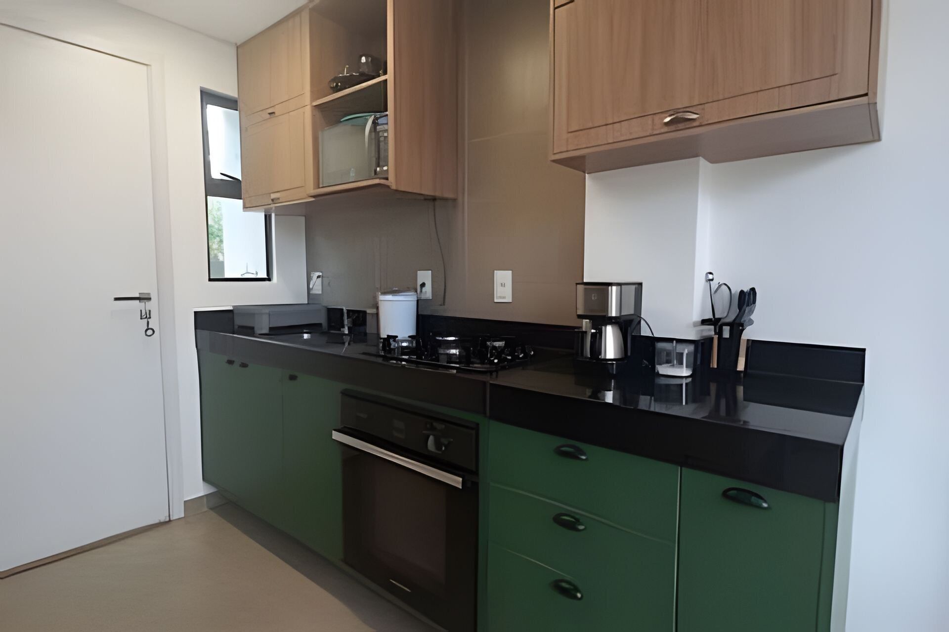 Uma cozinha moderna com armários verdes, bancada preta e eletrodomésticos de aço inoxidável.