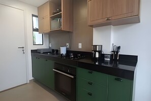 Uma cozinha moderna com armários verdes, bancada preta e eletrodomésticos de aço inoxidável.
