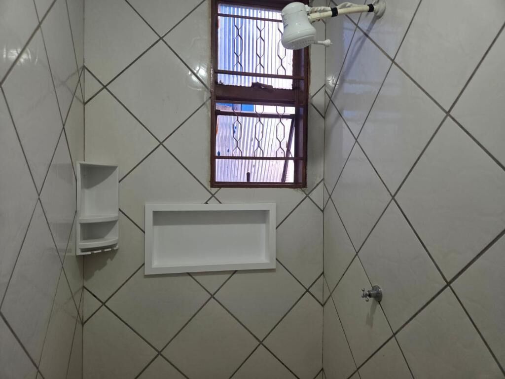 Um banheiro com janela, prateleira e vaso sanitário.