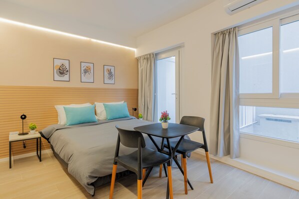 Quarto de hotel moderno com cama, mesa de cabeceira, luminária, planta em vaso e janela com cortinas.