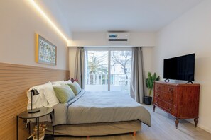 Quarto com cama, mesa de cabeceira, cômoda, televisão e varanda com vista.