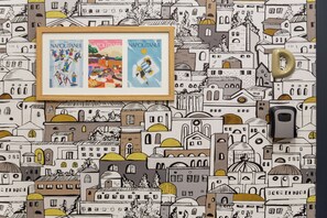 Uma moldura com capas da revista 'The Napolitaner' numa parede com um detalhado cenário urbano ao fundo.