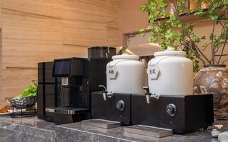 Uma estação de café com uma máquina de café, dois recipientes grandes e uma planta decorativa.