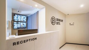 Uma área de recepção com um monitor exibindo imagens de vigilância, um balcão de recepção identificado como 'RECEPTION' e uma placa indicando um estacionamento.