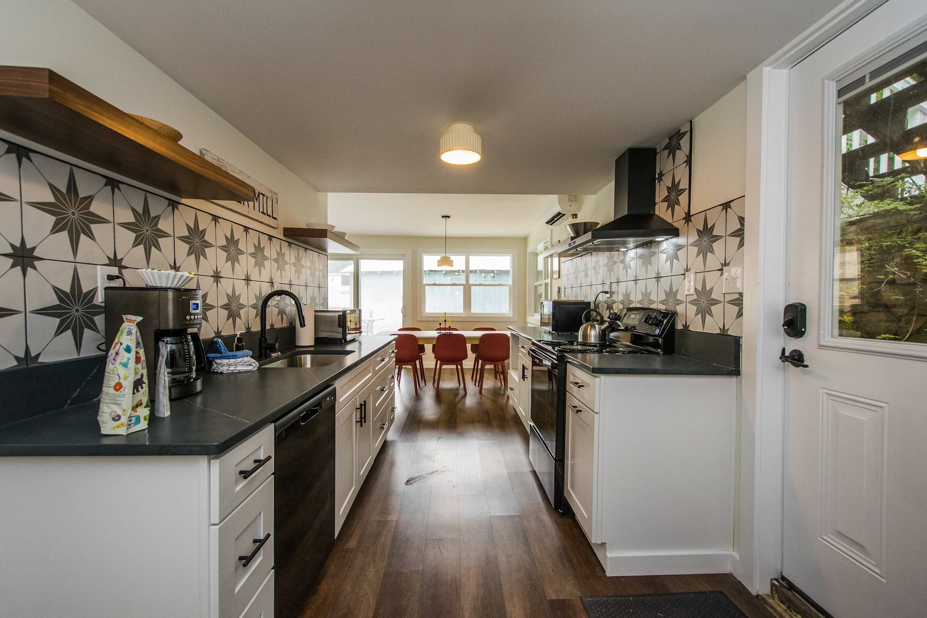 Uma cozinha com ilha central, armários brancos e backsplash estampado.
