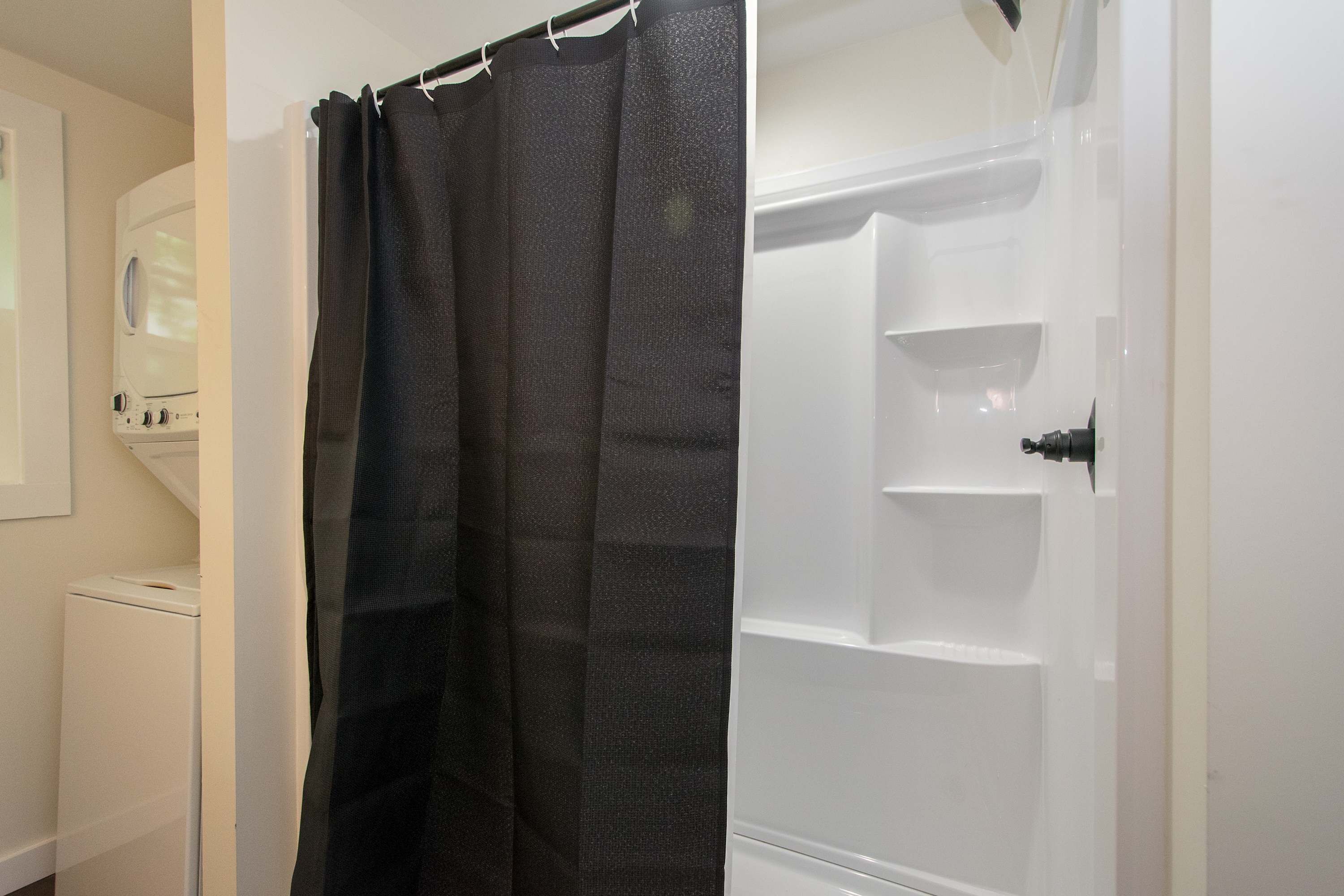 Casa de banho com cortina de chuveiro, porta branca e máquina de lavar roupa branca.