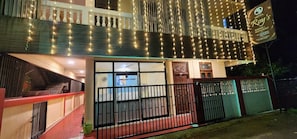 Um hotel com área de recepção, varanda decorada com luzinhas e placa indicando quartos e restaurante.