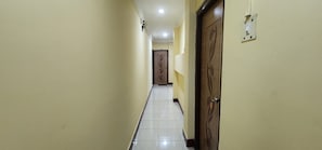 Um corredor estreito com piso de azulejos, uma porta com detalhe decorativo e um interruptor de luz na parede.