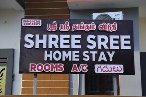 Placa com a inscrição 'SHREE SREE HOME STAY', números de contato e 'QUARTOS COM AR'.