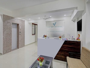 Uma área de recepção de hotel com balcão, televisão, sala de conferências e escadaria.