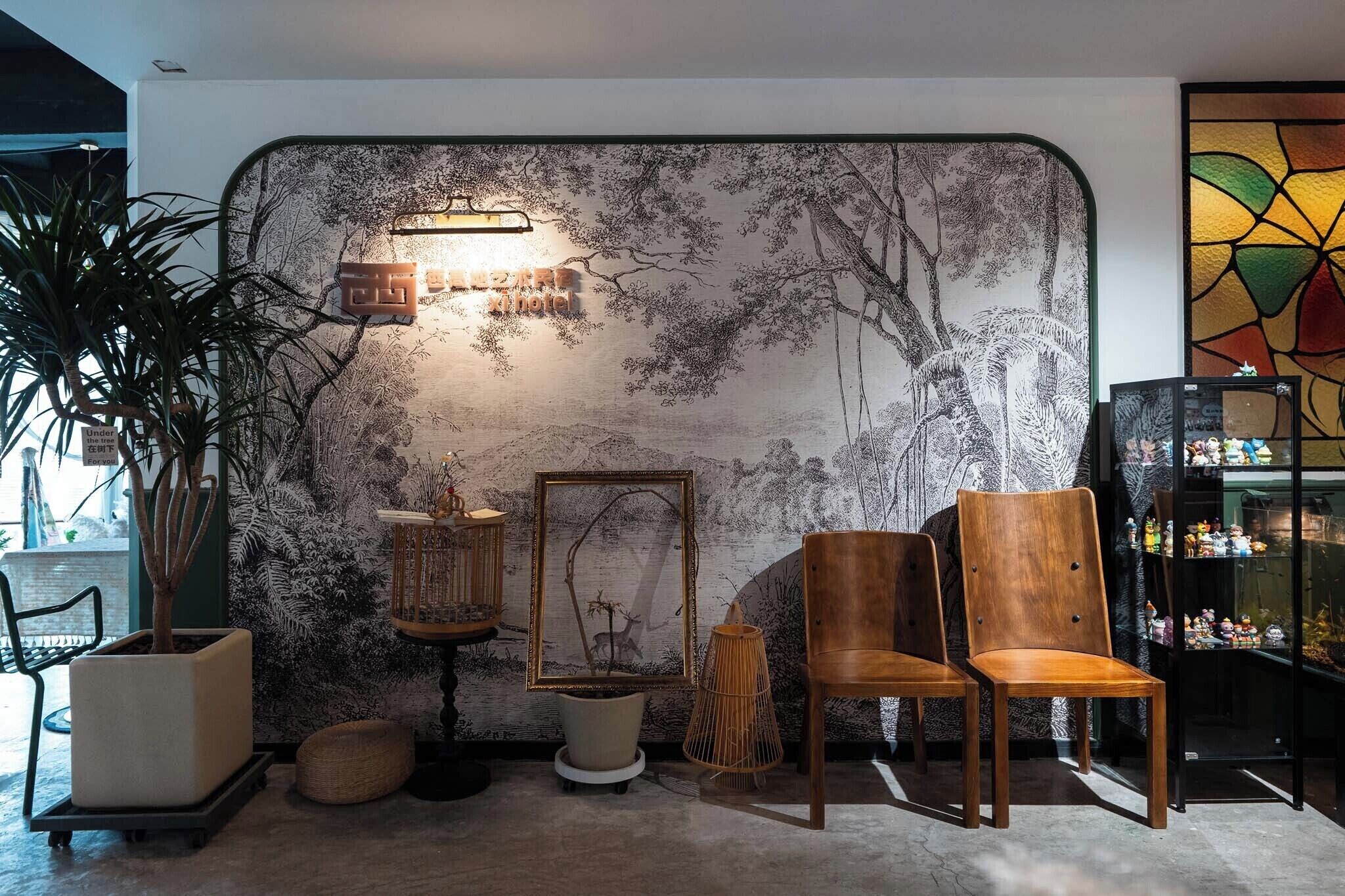 Quarto com um grande mural na parede, uma cadeira de madeira, uma mesa pequena e uma estante com objetos decorativos.
