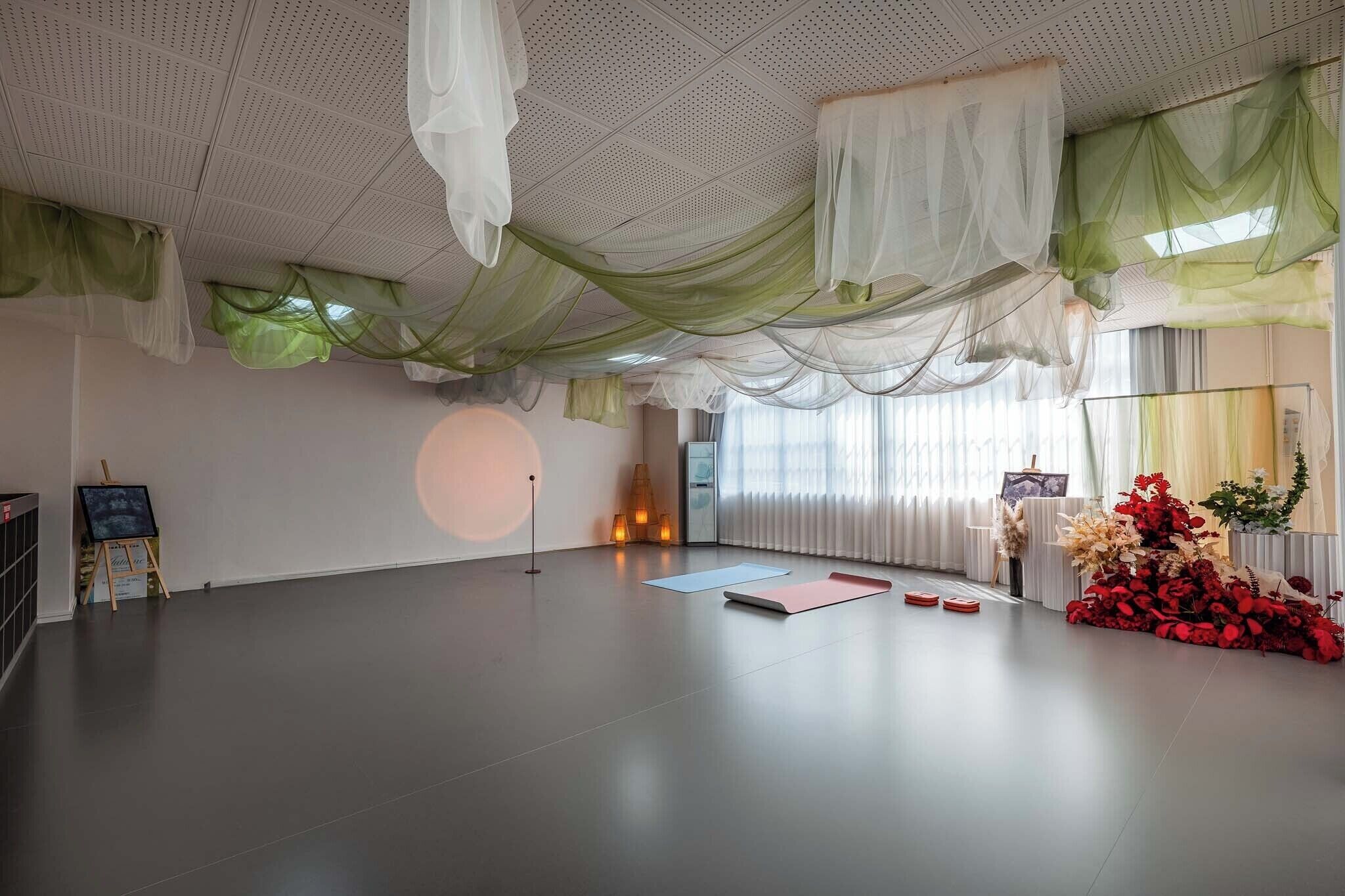 Um quarto amplo com teto branco, luminária circular grande e um arranjo floral à direita.
