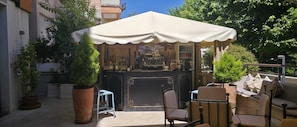 Um café com toldo branco, mesas ao ar livre e um balcão de bar.