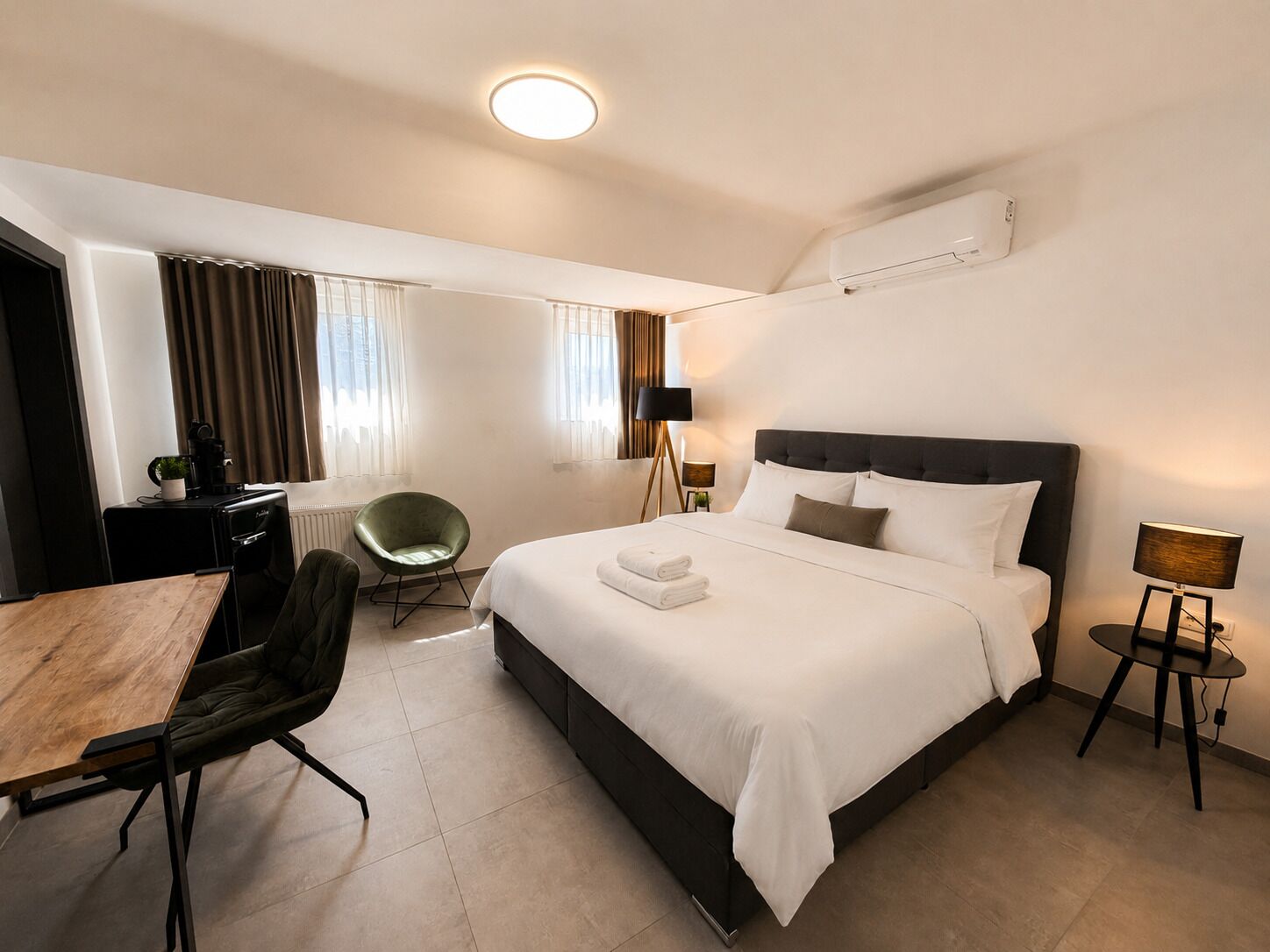 Quarto de hotel com cama, escrivaninha, cadeira, abajur e aparelho de ar condicionado.